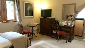 Quarto de hotel com duas camas, uma escrivaninha com computador, uma cadeira, cômoda, espelho e janela com cortinas.