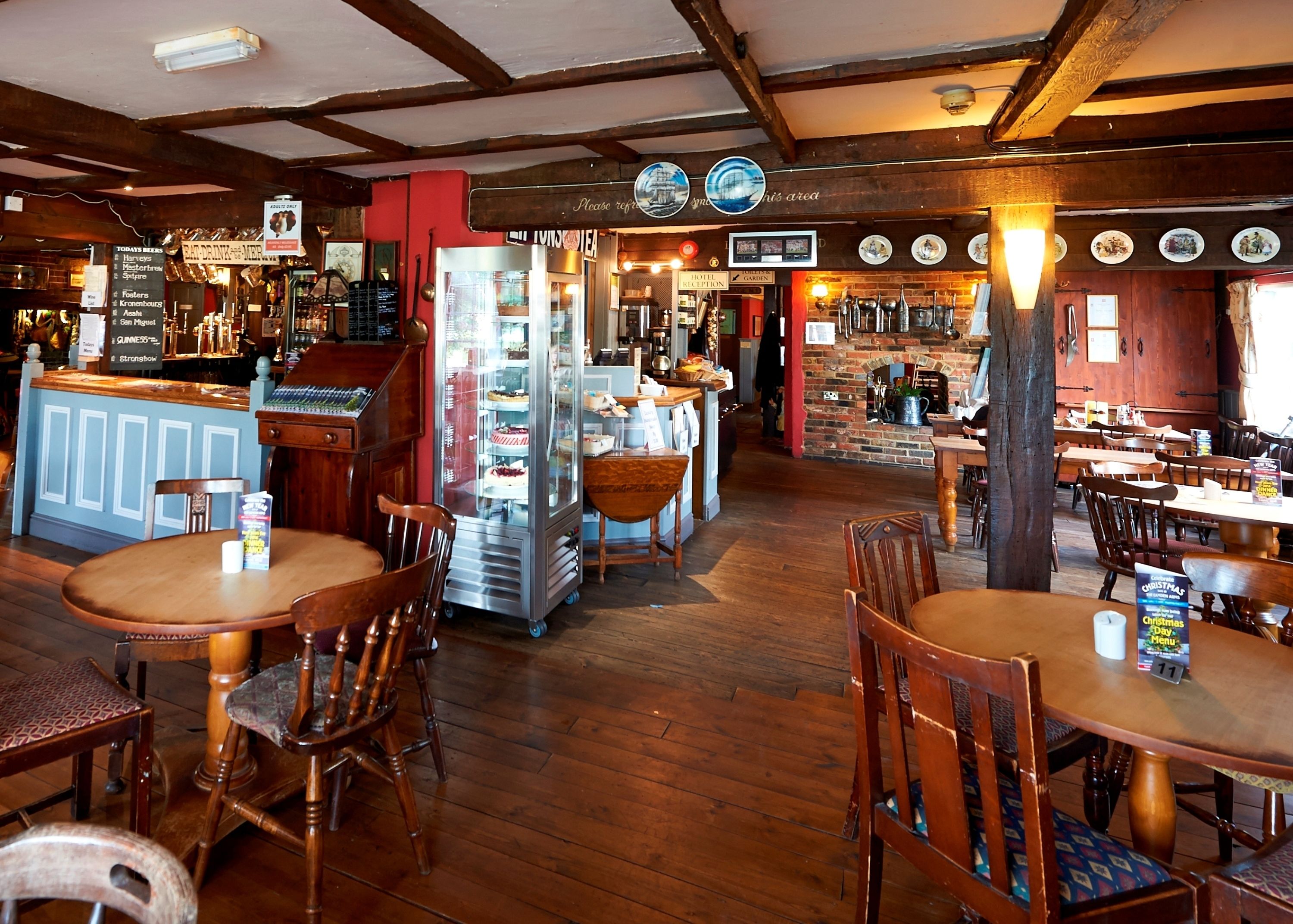 Um restaurante acolhedor com pisos e mesas de madeira, uma área de bar e uma vitrine com sobremesas.