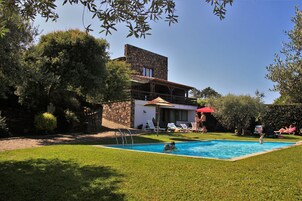 Uma casa com piscina, cercada por um gramado bem cuidado e árvores.