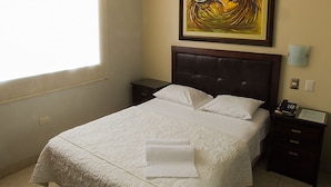 Uma cama bem arrumada com um edredom branco, uma mesa de cabeceira com abajur e um quadro na parede.