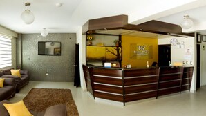 Uma área de recepção de hotel com um balcão de madeira, um espelho grande e um espaço de estar com sofás.