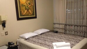 Quarto de hotel com colcha estampada em padrão de zebra, um quadro na parede e uma janela com cortinas.