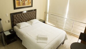 Quarto de hotel com uma cama grande, uma mesa de cabeceira com telefone, uma pequena escrivaninha com computador e uma cadeira.
