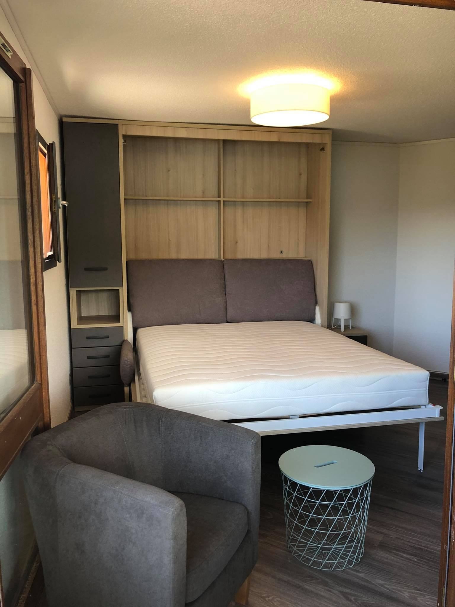 Quarto com cama, uma cadeira, mesa de cabeceira, abajur e uma pequena mesa redonda.