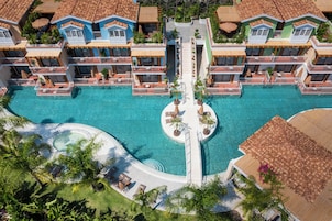Resort com vários edifícios, piscina central e palmeiras ao redor.