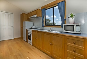 Cozinha com armários de madeira, fogão, micro-ondas e janela com cortinas.