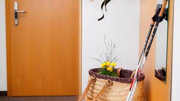 Um quarto com porta de madeira, uma cesta de vime com flores, uma bengala e um par de botas no chão.