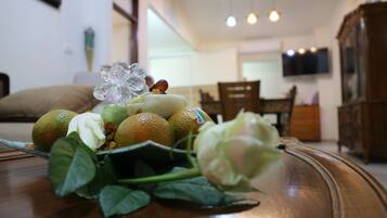 Uma tigela de frutas com frutas cítricas e uma flor sobre uma mesa de madeira em um quarto com televisão e móveis.