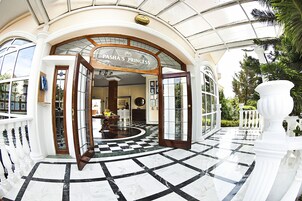 Uma entrada imponente com piso de mármore quadriculado, uma placa com a inscrição 'Pasha's Princess' e uma porta de vidro que dá acesso ao interior.