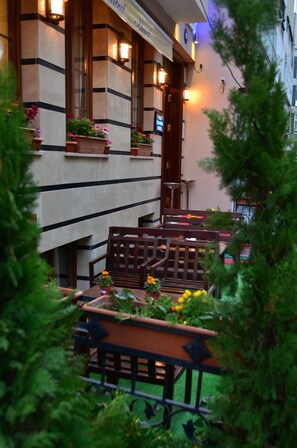 Um pátio com um banco de madeira, plantas em vasos e um edifício com uma placa.
