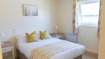Quarto com cama, mesas de cabeceira, abajur, janela com cortinas e uma obra de arte na parede.