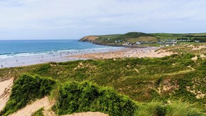 Uma praia costeira com areal, dunas gramadas e um pequeno povoado com casas.