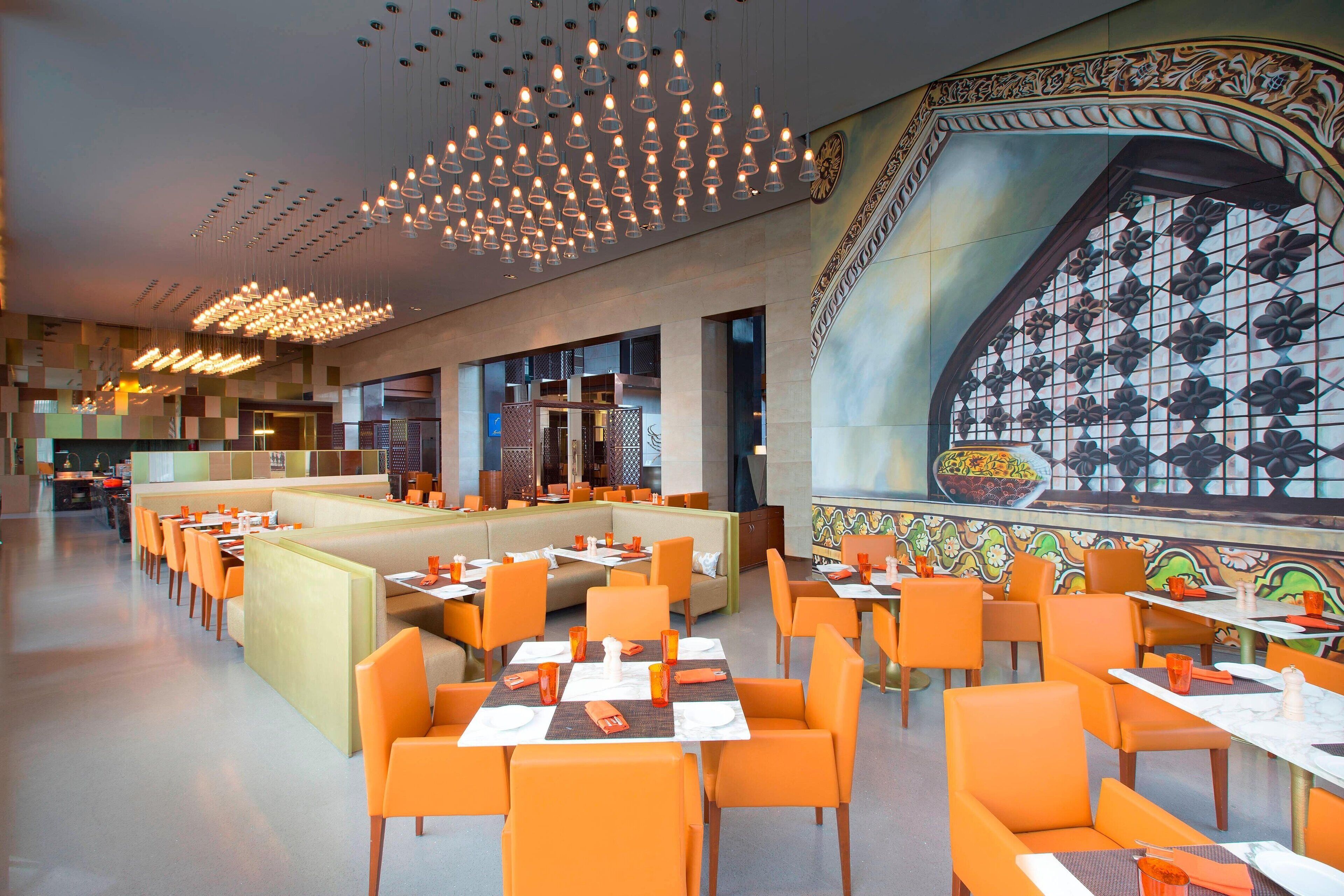Um restaurante moderno com assentos laranja, um mural decorativo e um lustre único.