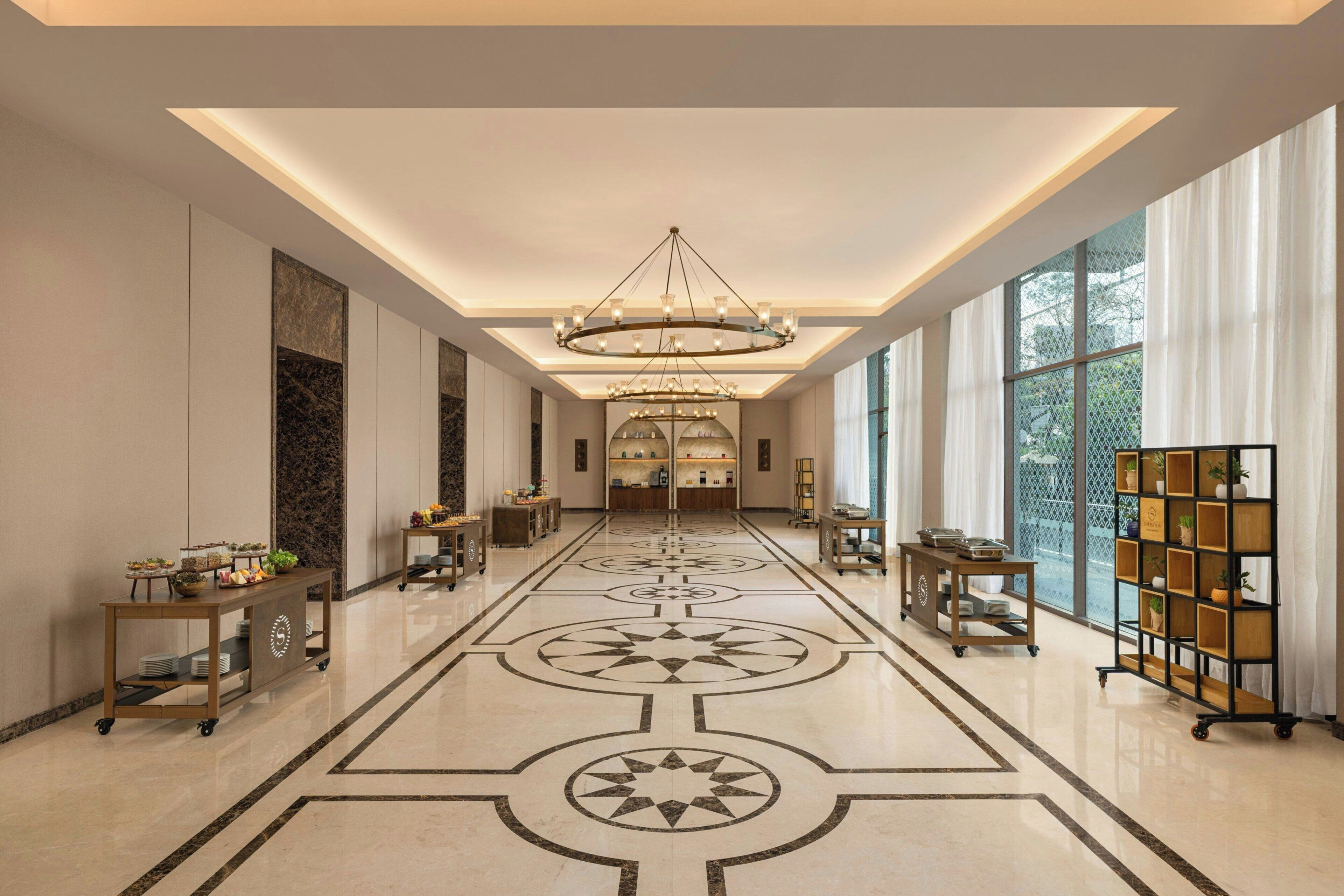 Corredor de hotel com lustre, balcão de recepção e disposição para buffet.
