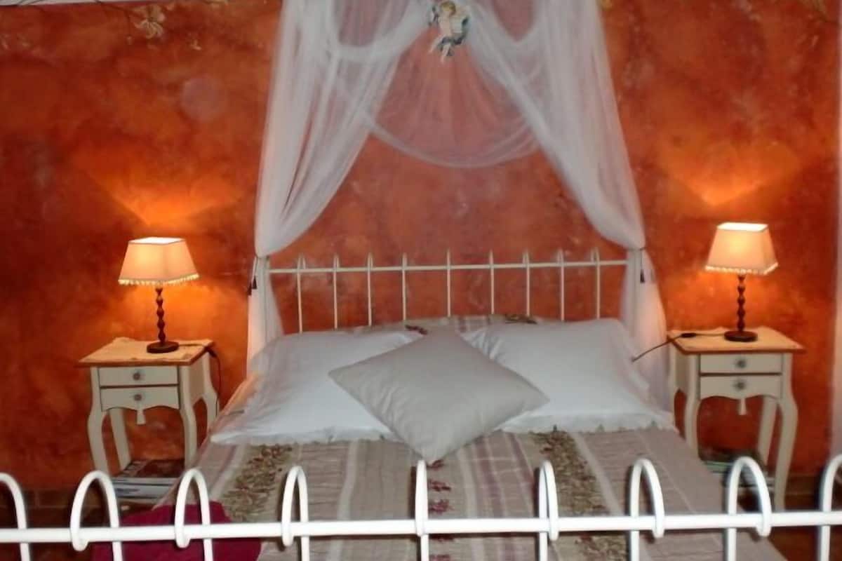 Quarto com cama, duas mesas de cabeceira, dossel e parede decorativa.