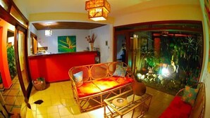 Quarto com sofá vermelho, mesa pequena, luminária pendente, quadro e um aquário grande.
