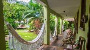 Área externa coberta com rede, cadeiras e vista para um jardim exuberante.