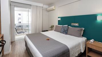 Quarto de hotel com cama, mesa de cabeceira com telefone, janela com cortinas e vista para o exterior.