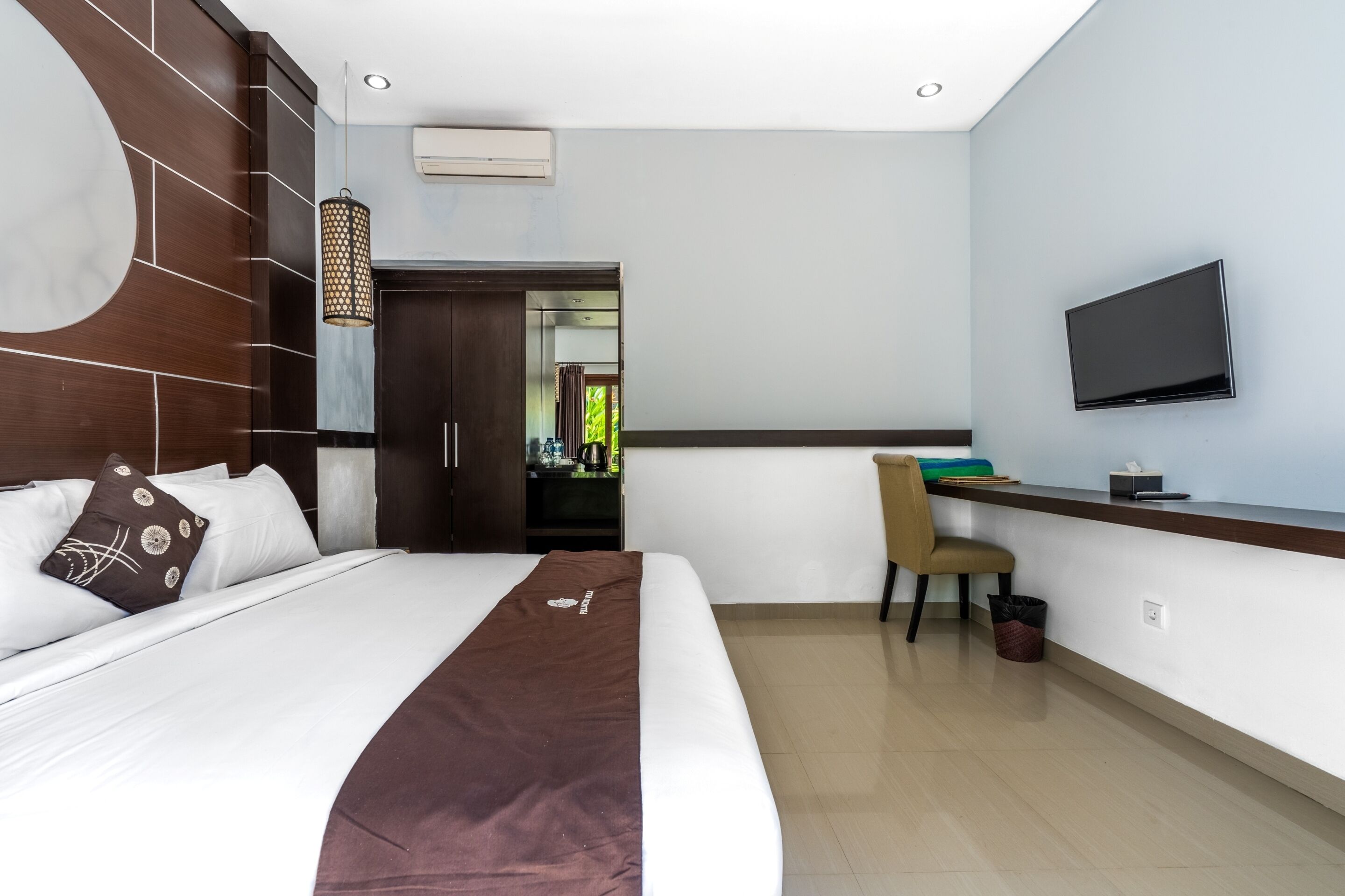 Quarto de hotel moderno com uma cama grande, uma escrivaninha, uma cadeira, uma televisão e um espelho.