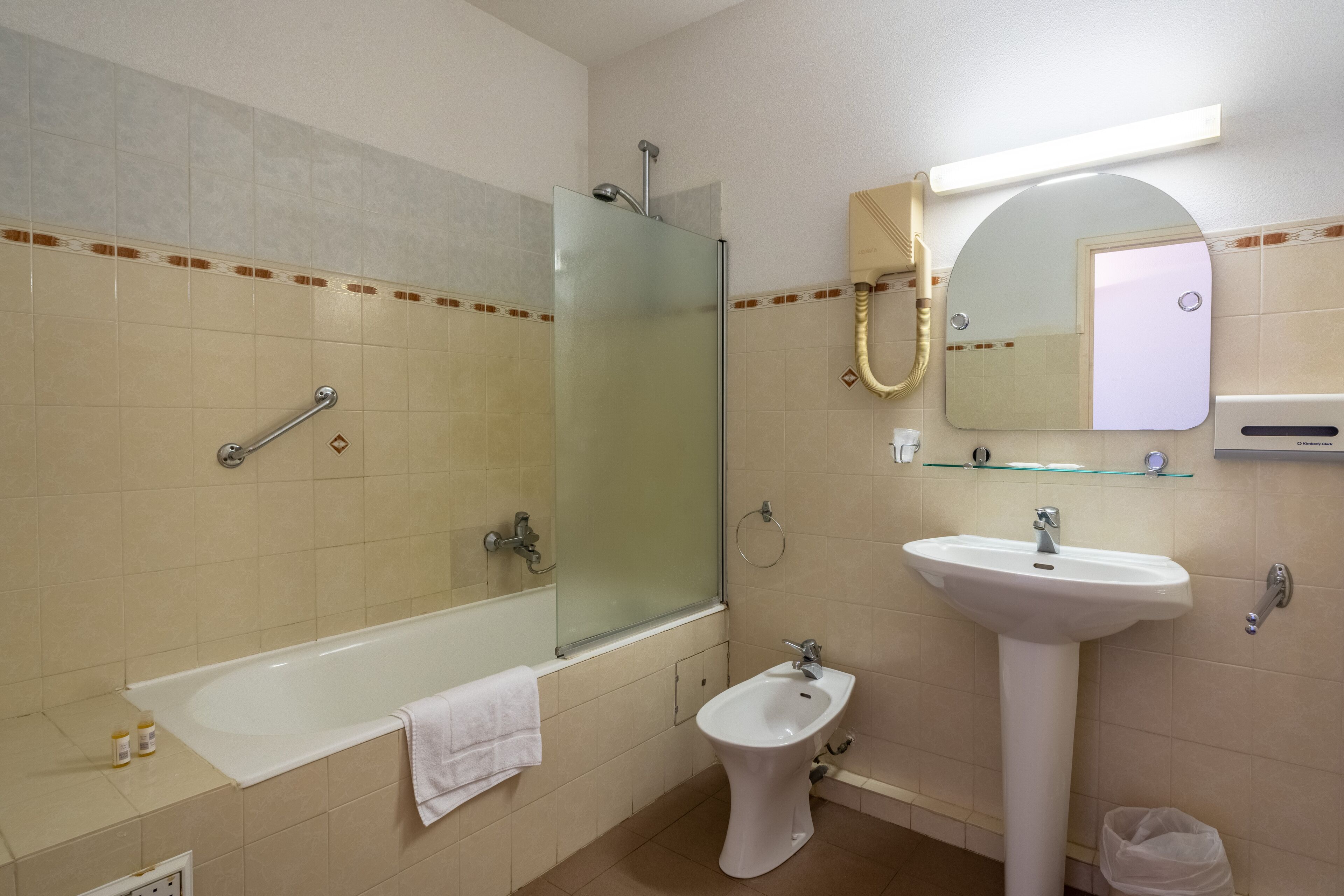 Casa de banho com banheira, cabine de chuveiro com paredes de vidro, lavatório suspenso e espelho.
