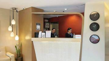 Bancada de recepção de hotel com dois funcionários, um relógio e uma caixa para gorjetas.