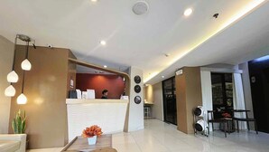 Um lobby de hotel moderno com uma mesa de recepção, uma área de refeições com banquetas de madeira e uma área de estar com um sofá.
