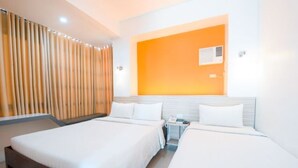 Quarto de hotel com duas camas, cortina de madeira, parede de destaque laranja e uma pequena mesa de cabeceira com telefone.
