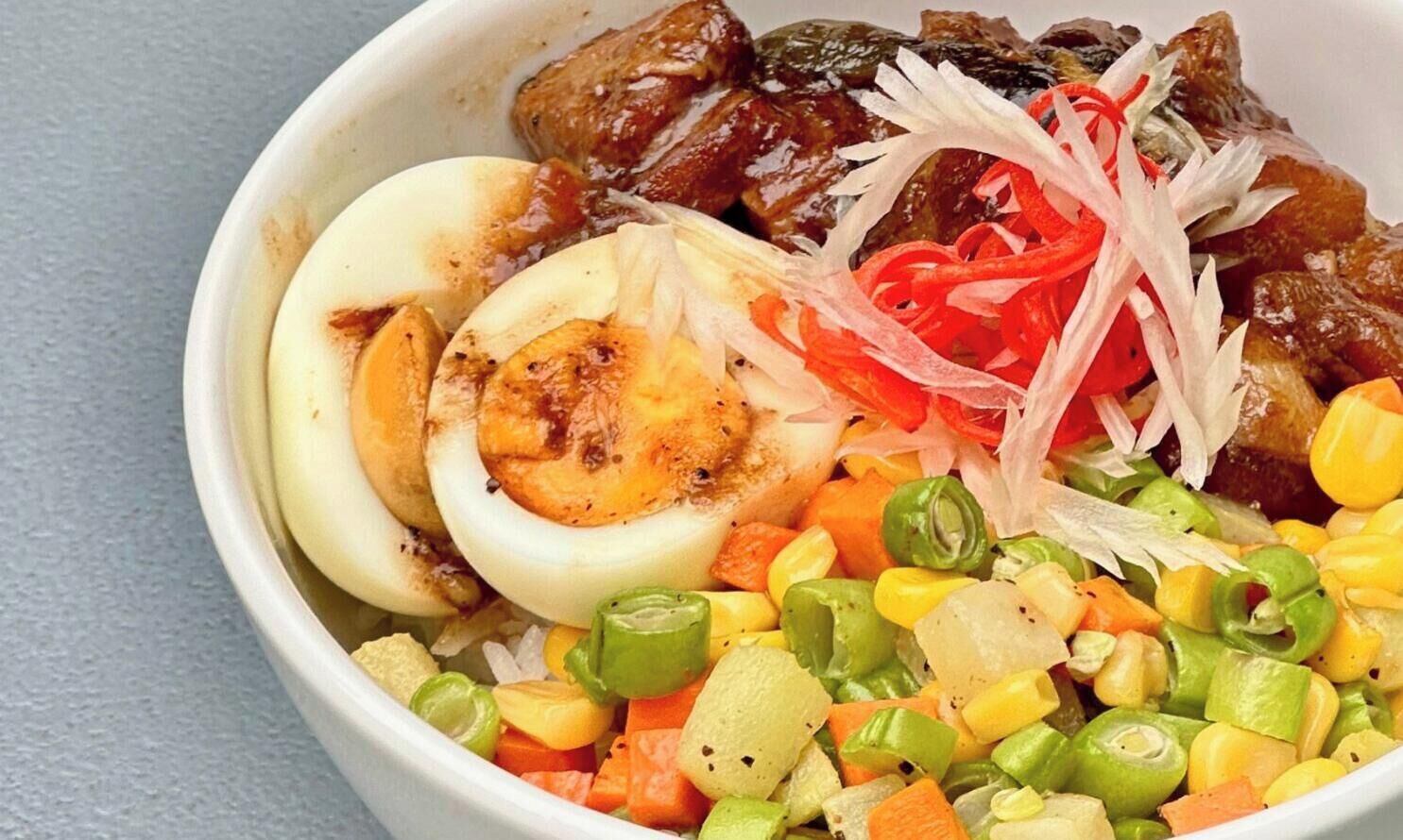 Uma tigela de comida com diversos ingredientes, incluindo ovos cozidos, legumes e carne.