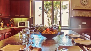 Uma cozinha com uma mesa de jantar posta para quatro pessoas, uma tigela de frutas e um relógio na parede.