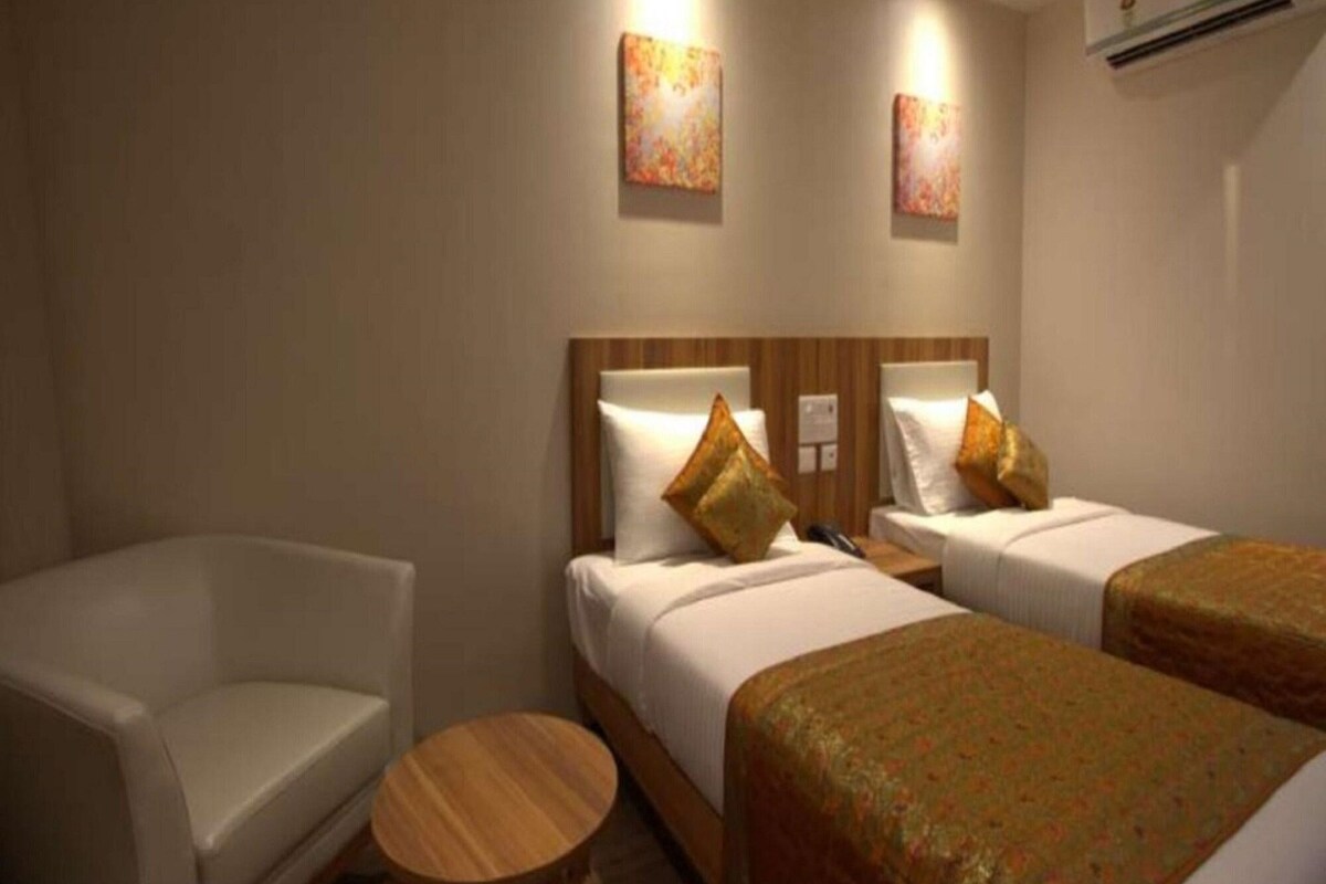Quarto de hotel com duas camas, uma cadeira e uma mesa redonda pequena.