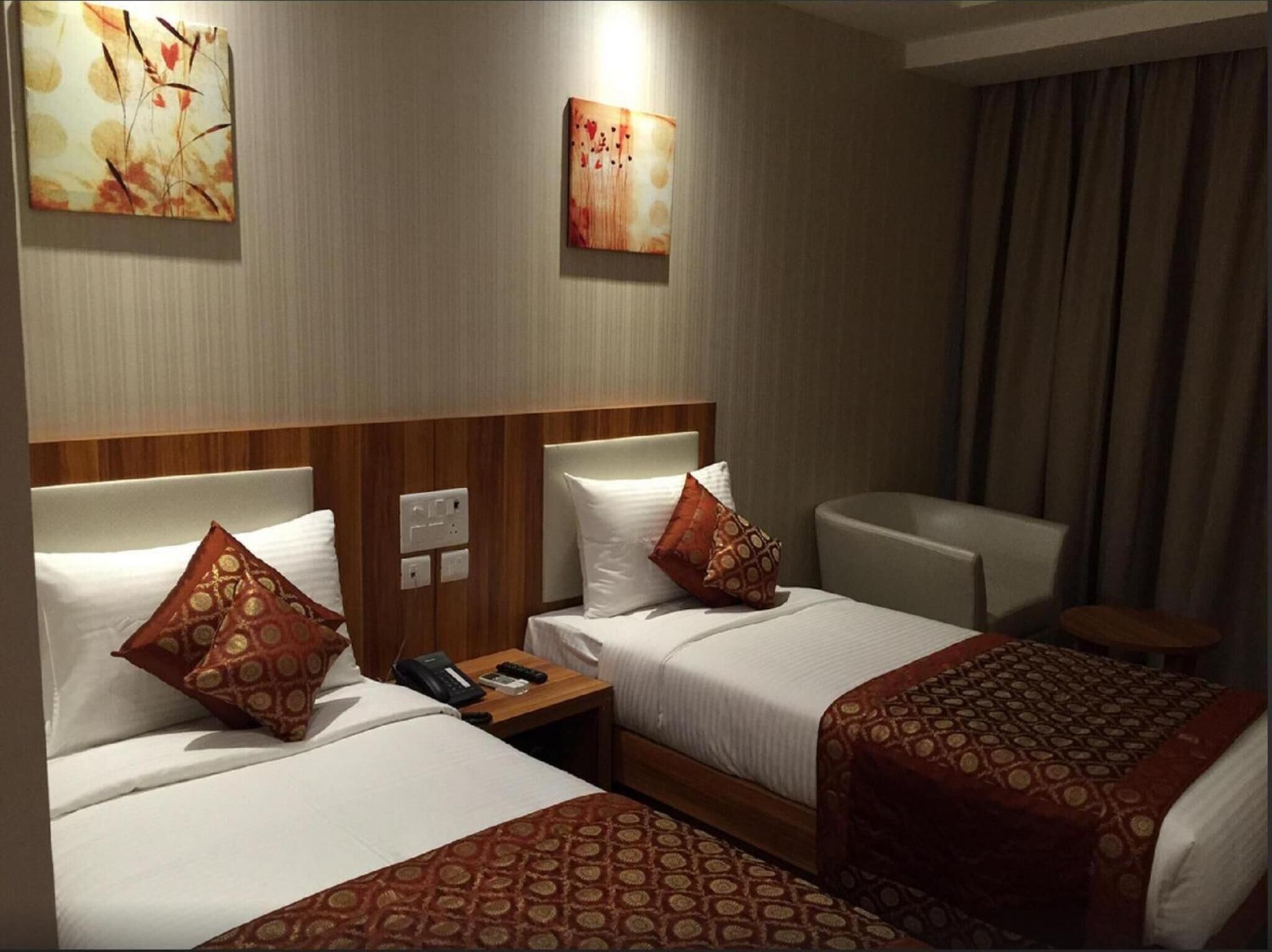 Quarto de hotel com duas camas, uma mesa de cabeceira com telefone e controle remoto, e obras de arte nas paredes.