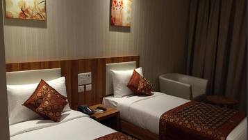 Quarto de hotel com duas camas, uma mesa de cabeceira com telefone e controle remoto, e obras de arte nas paredes.