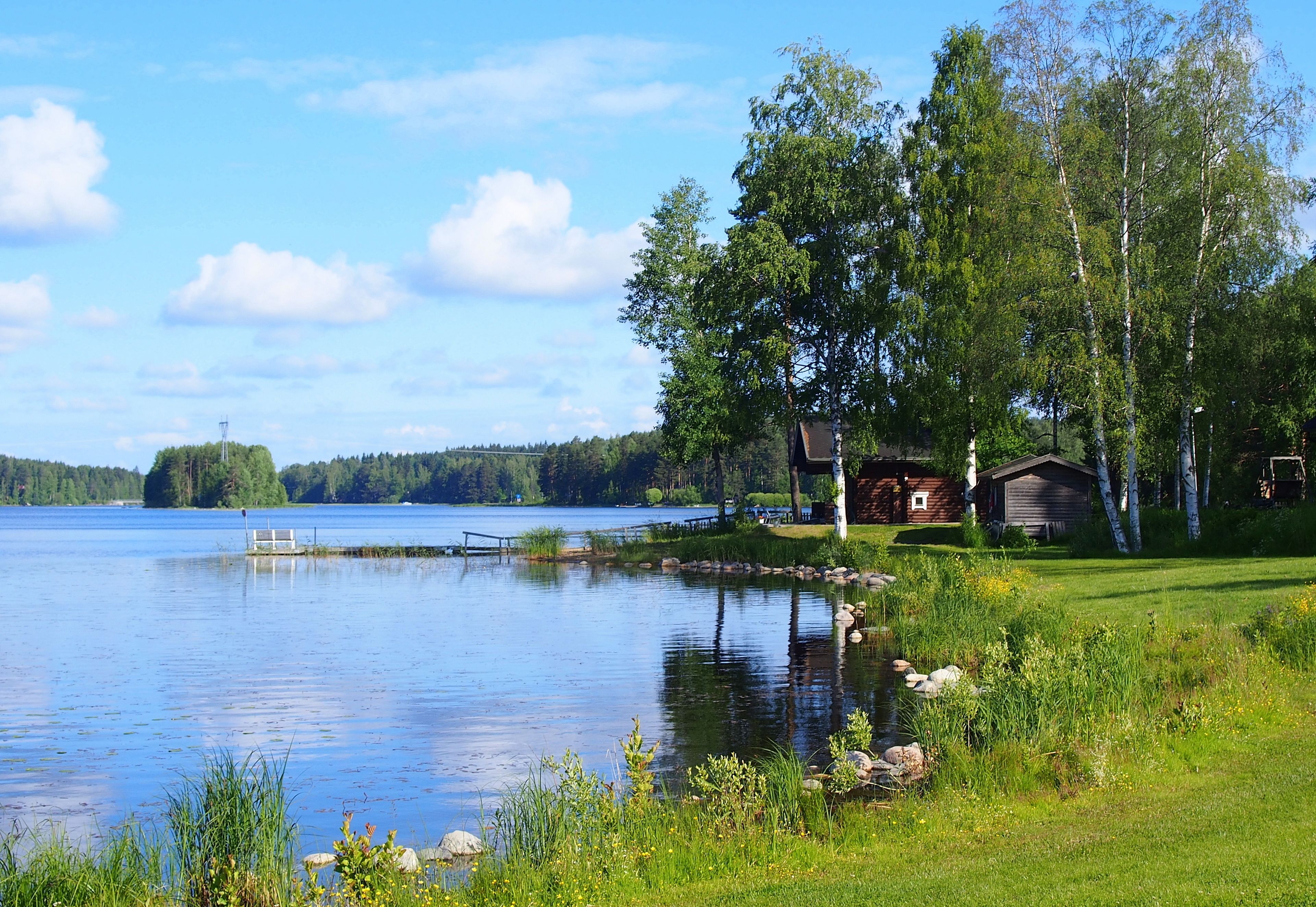 Uma cabana à beira de um lago, com um cais, rodeada por vegetação exuberante e árvores.