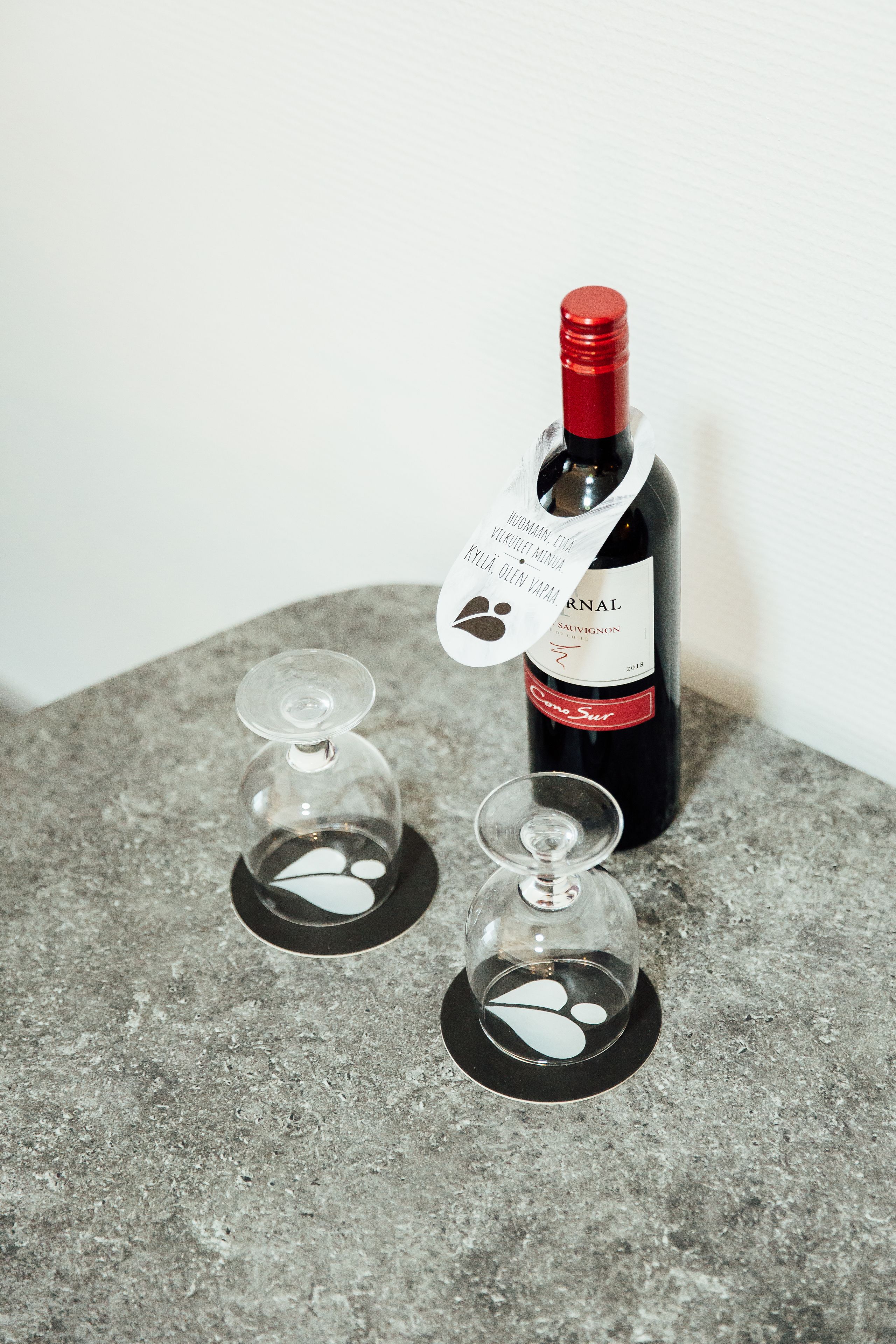 Uma garrafa de vinho com etiqueta, sobre uma superfície de pedra com dois copos de vinho.