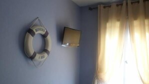 Quarto com um círculo salva-vidas na parede, uma pequena luminária e uma janela com cortinas.