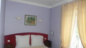 Quarto com cama, mesa de cabeceira, luminária na parede e janela com cortinas.