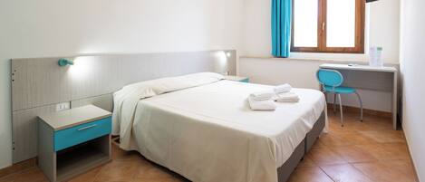 Um quarto com cama, escrivaninha, cadeira e mesa de cabeceira.