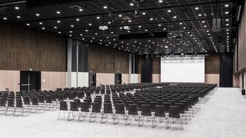 Uma grande sala de conferências com fileiras de cadeiras, uma tela de projetor e um palco.