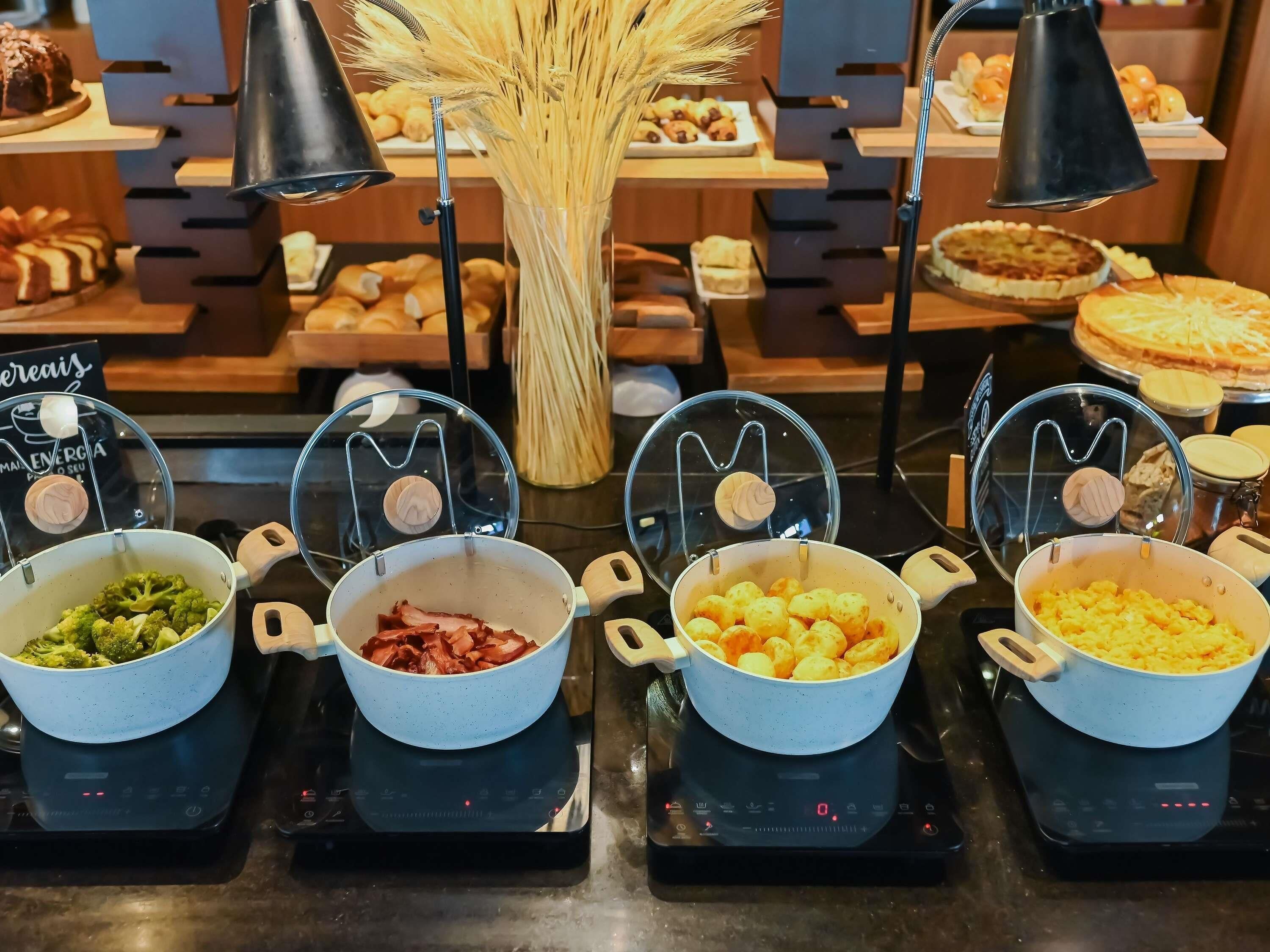 Buffet com diversos alimentos em panelas sobre cooktops por indução, rodeado por uma seleção de doces e sobremesas.