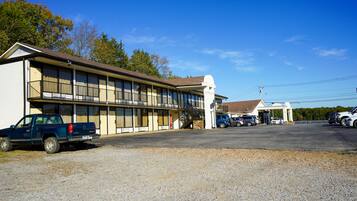 Um motel com um prédio de dois andares, área de estacionamento coberta e entrada com calçamento de brita.