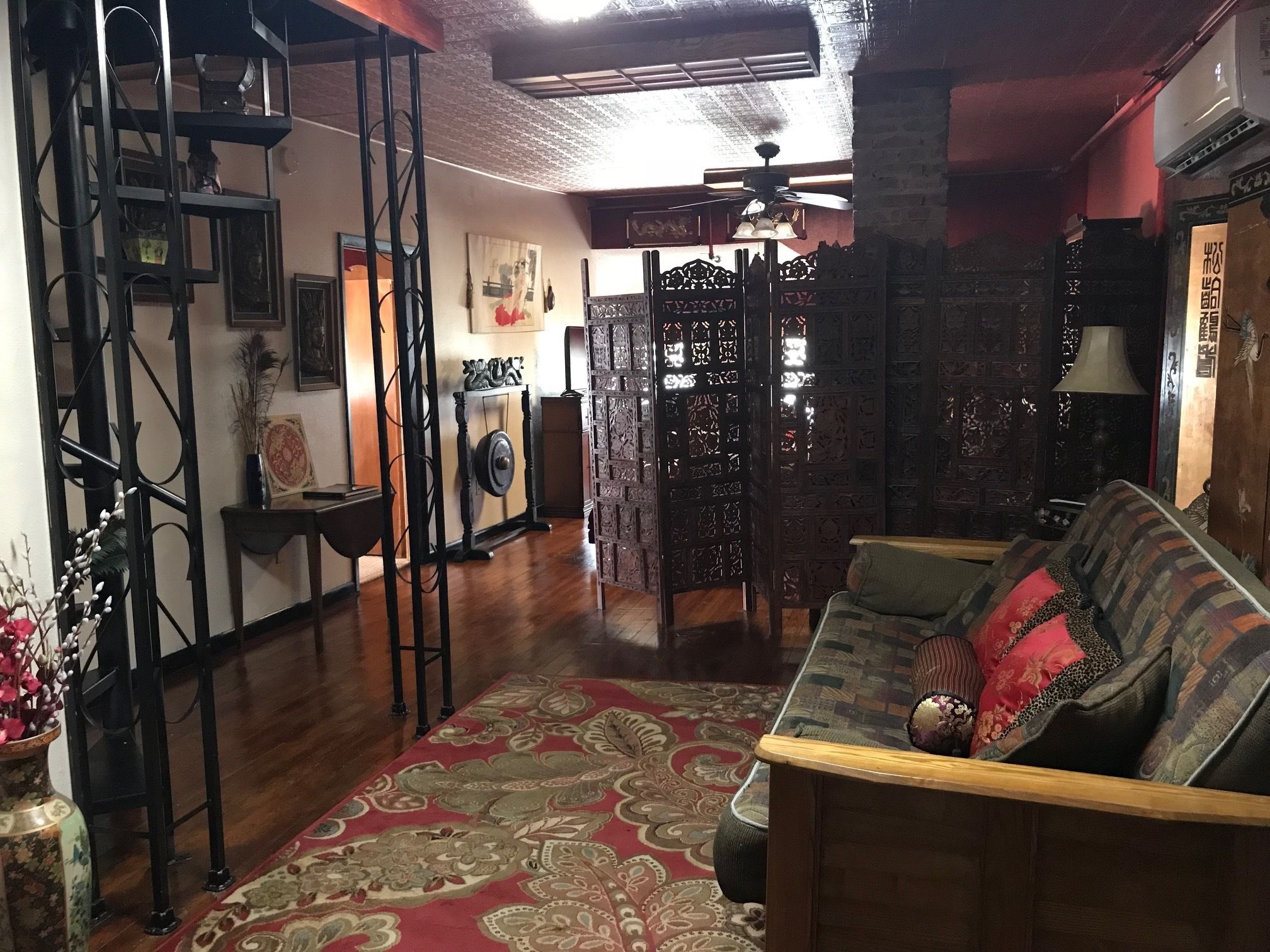 Uma sala de estar aconchegante com um tapete estampado, um sofá com almofadas decorativas, uma mesa de centro de madeira e um portão decorativo.