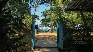 Um caminho de madeira leva a uma área de praia, cercado por vegetação exuberante e um portão azul.