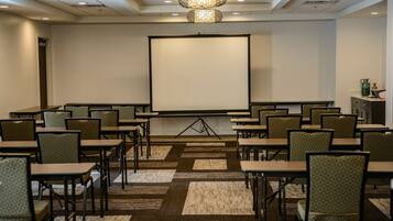 Uma sala de conferências com uma tela grande, várias mesas e cadeiras dispostas para uma reunião.