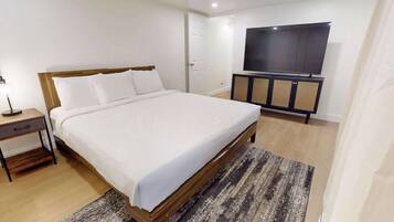 Quarto de hotel bem arrumado com uma cama grande, mesa de cabeceira com abajur, televisão em um suporte e um tapete estampado.