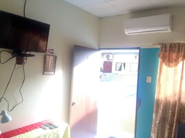Um quarto com televisão na parede, ar condicionado acima da porta e uma mesa com toalha vermelha e alguns objetos sobre ela.
