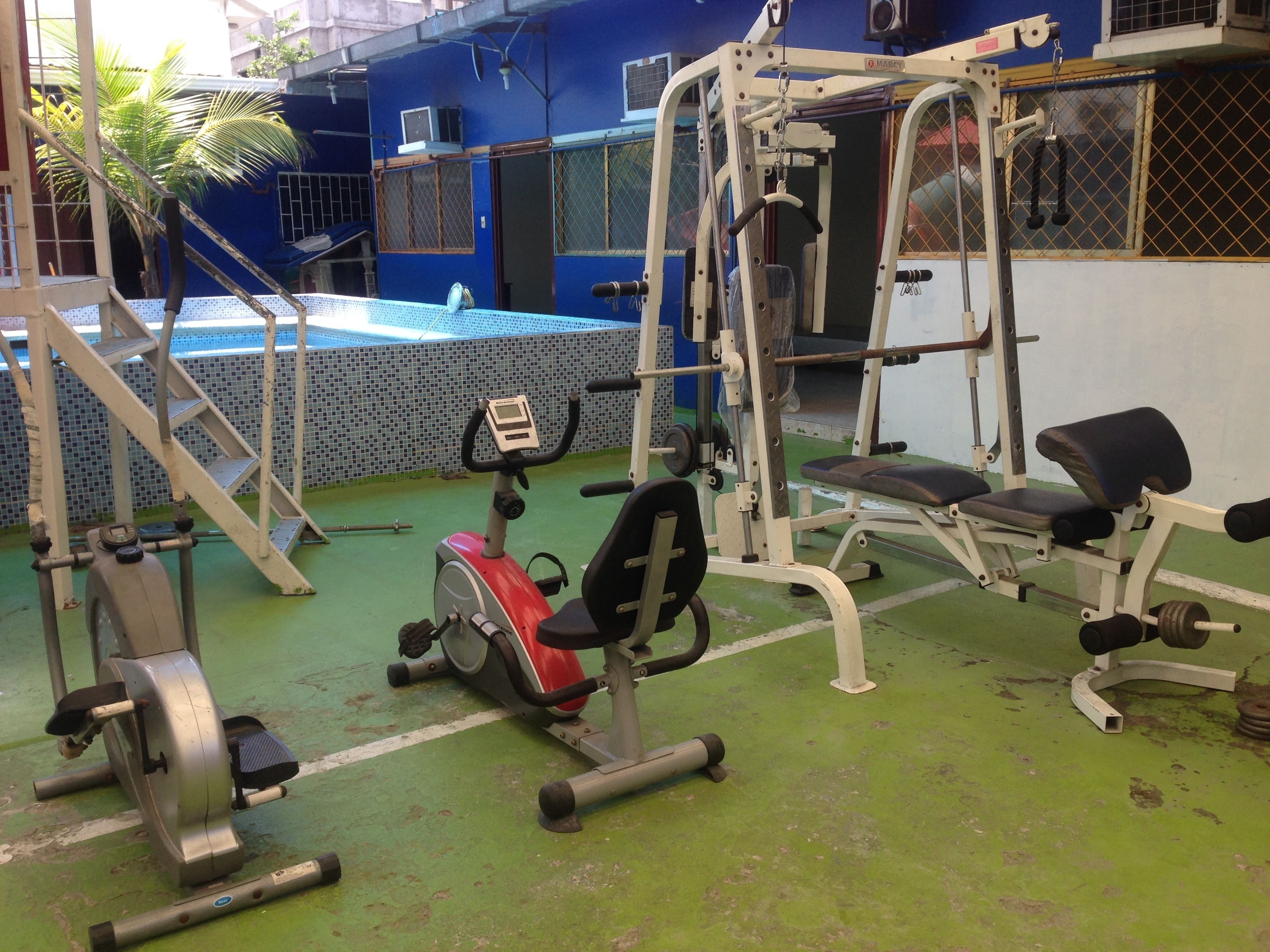 Uma academia com equipamentos de ginástica, piso verde e parede azul com janelas.