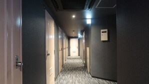 Um corredor de hotel com piso revestido de carpete, portas em ambos os lados e um respiradouro no teto.
