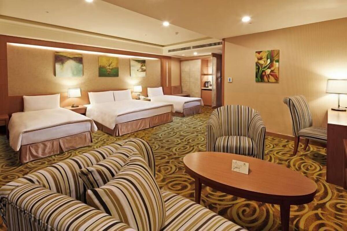 Quarto de hotel com três camas, um sofá, uma mesa e uma televisão.