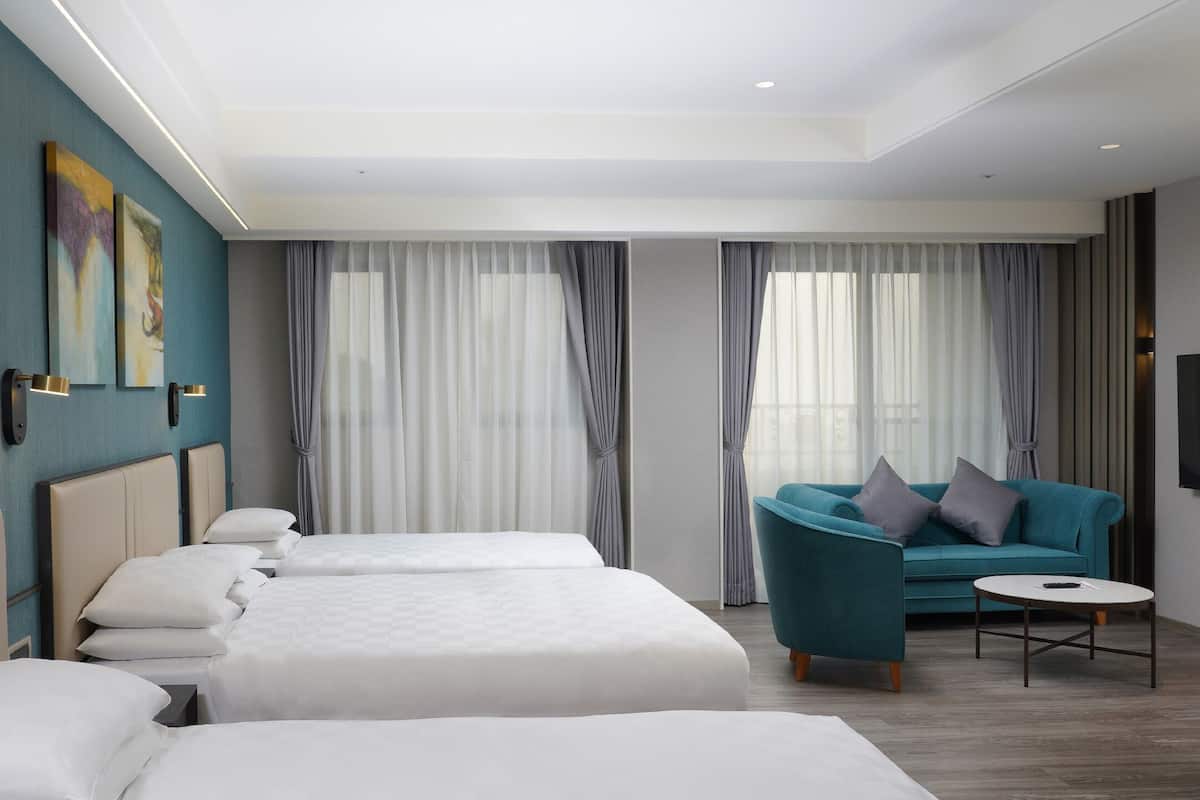 Quarto de hotel com duas camas, um sofá, uma TV e uma pequena mesa.