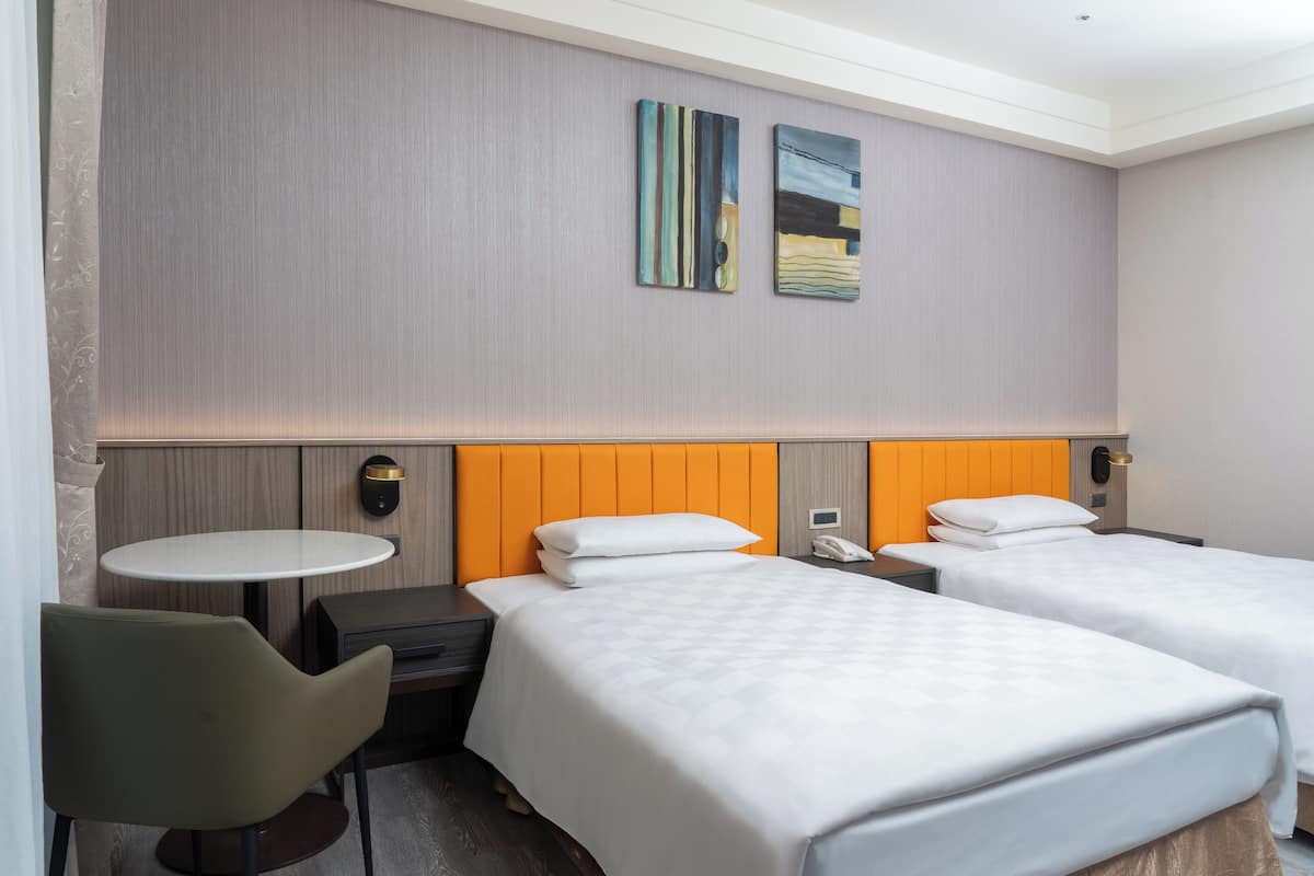 Quarto de hotel com duas camas, uma mesa redonda, uma cadeira e obras de arte na parede.